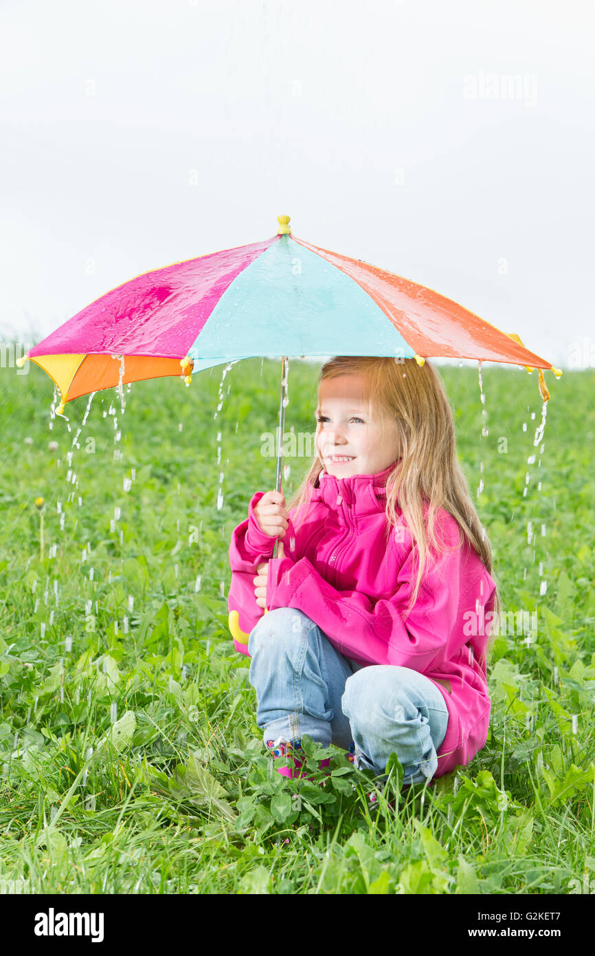 Young girl crouching with umbrella on meadow, rainy weather Stock Photo ...
