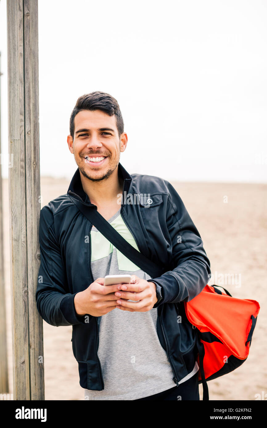 Portrait of smiling young man leaning against pole on the beach Stock ...