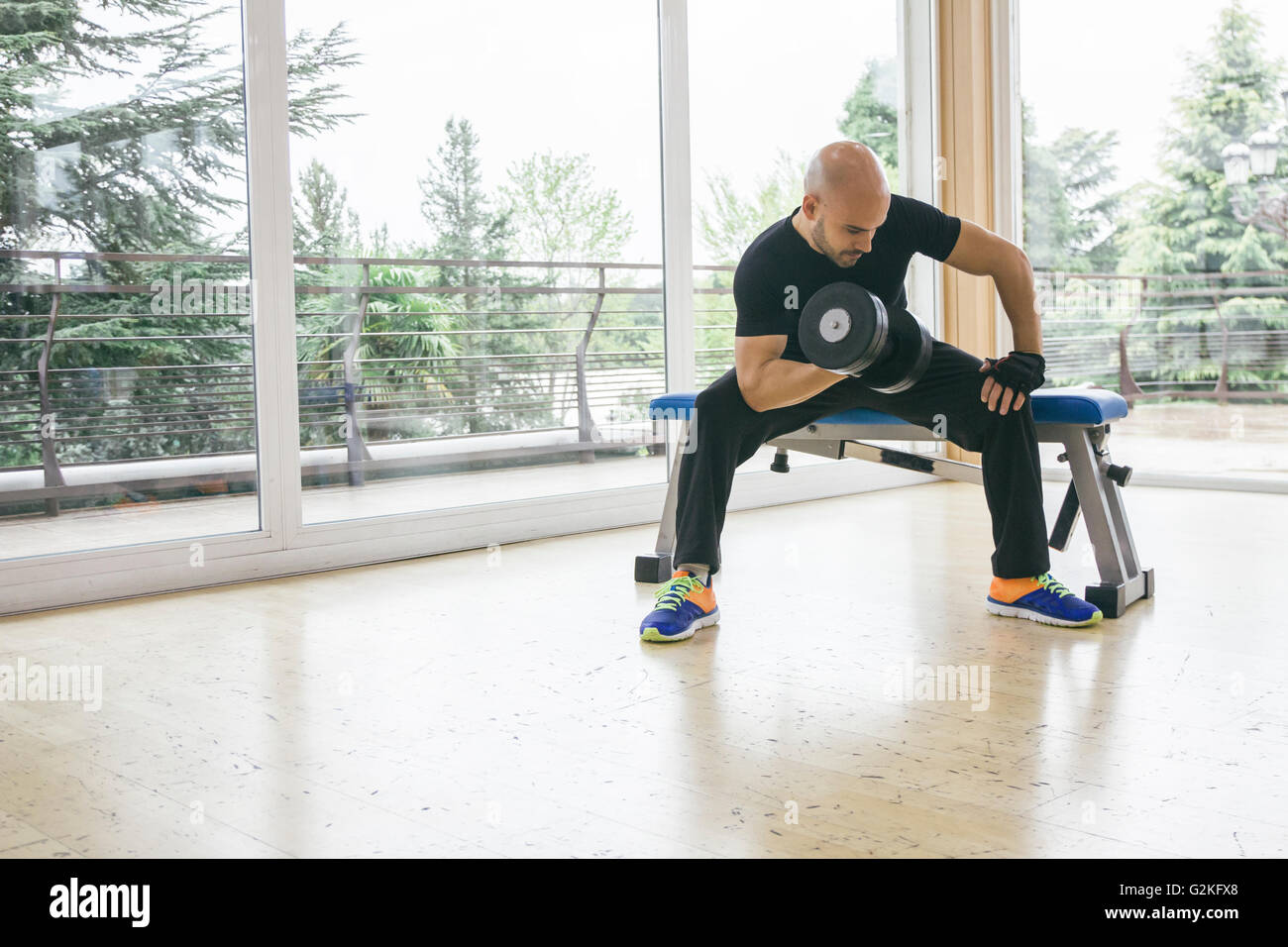 Man lifting a dumbbell sitting on a bench in a gym Stock Photo - Alamy