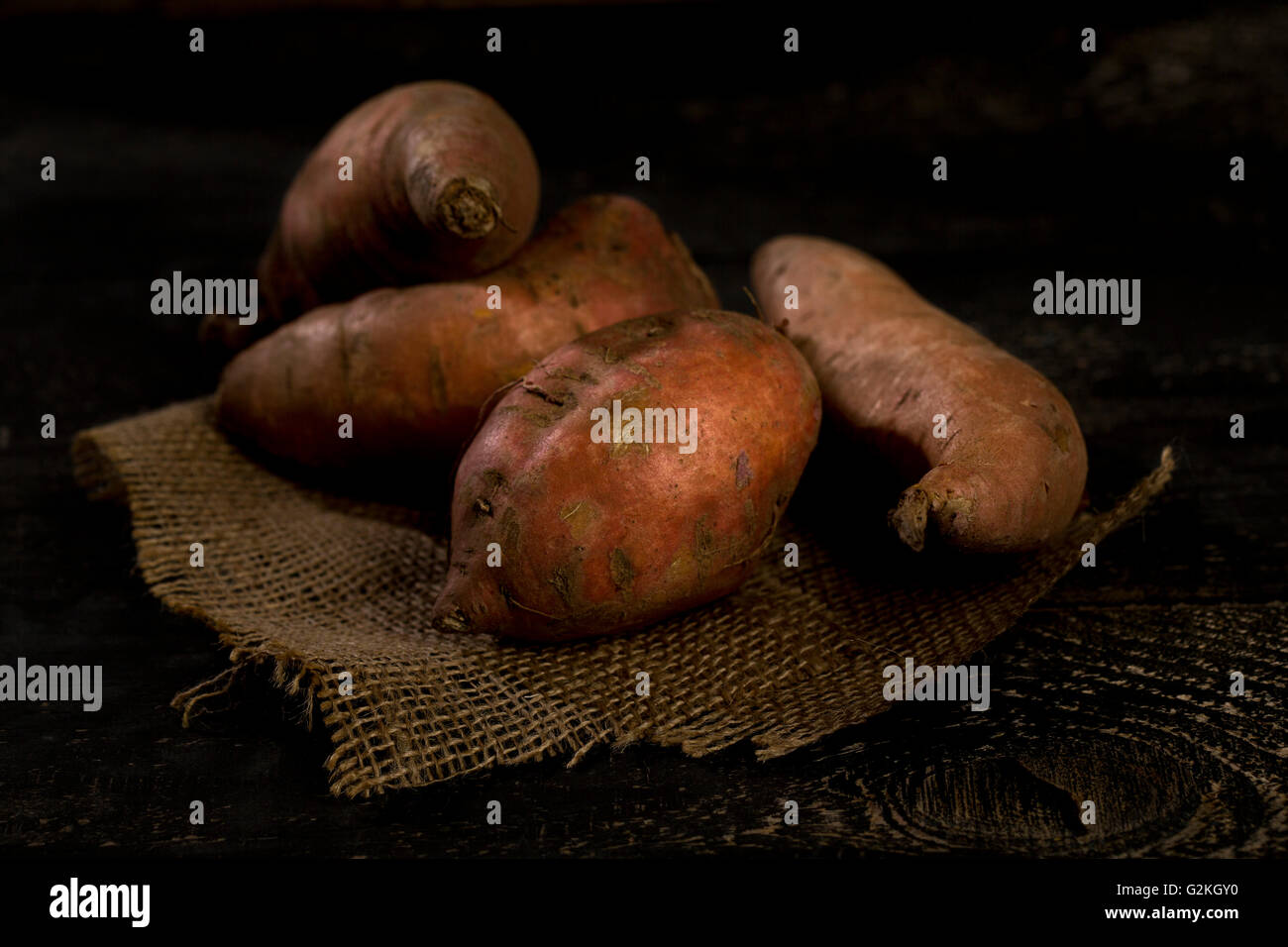 Four sweet potatoes on jute and dark wood Stock Photo - Alamy