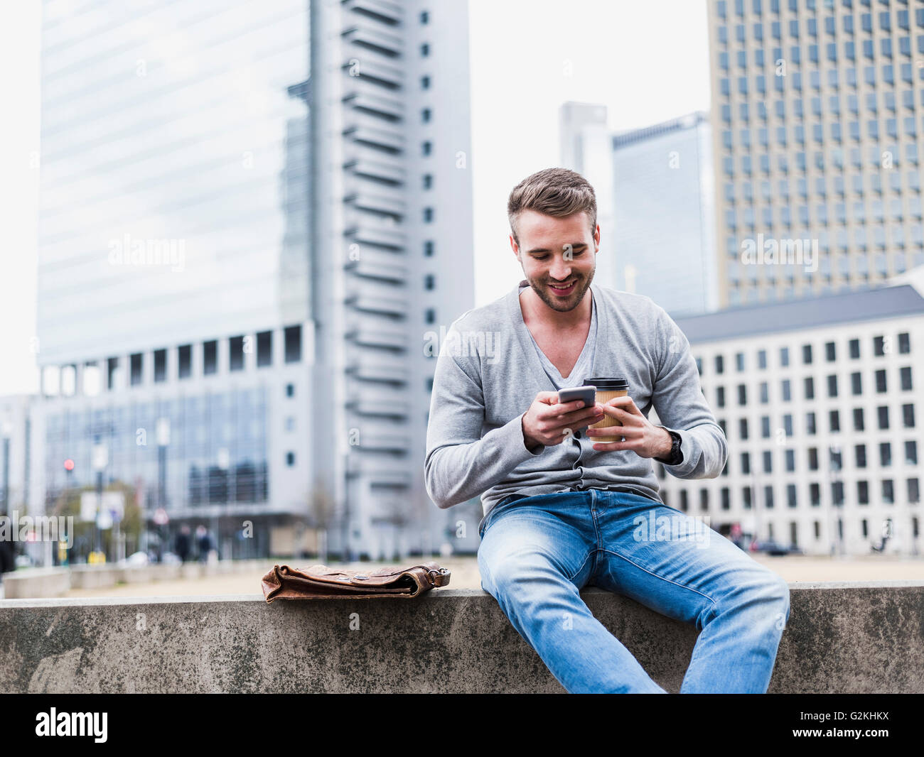 Young man sitting on wall reading text messages Stock Photo - Alamy