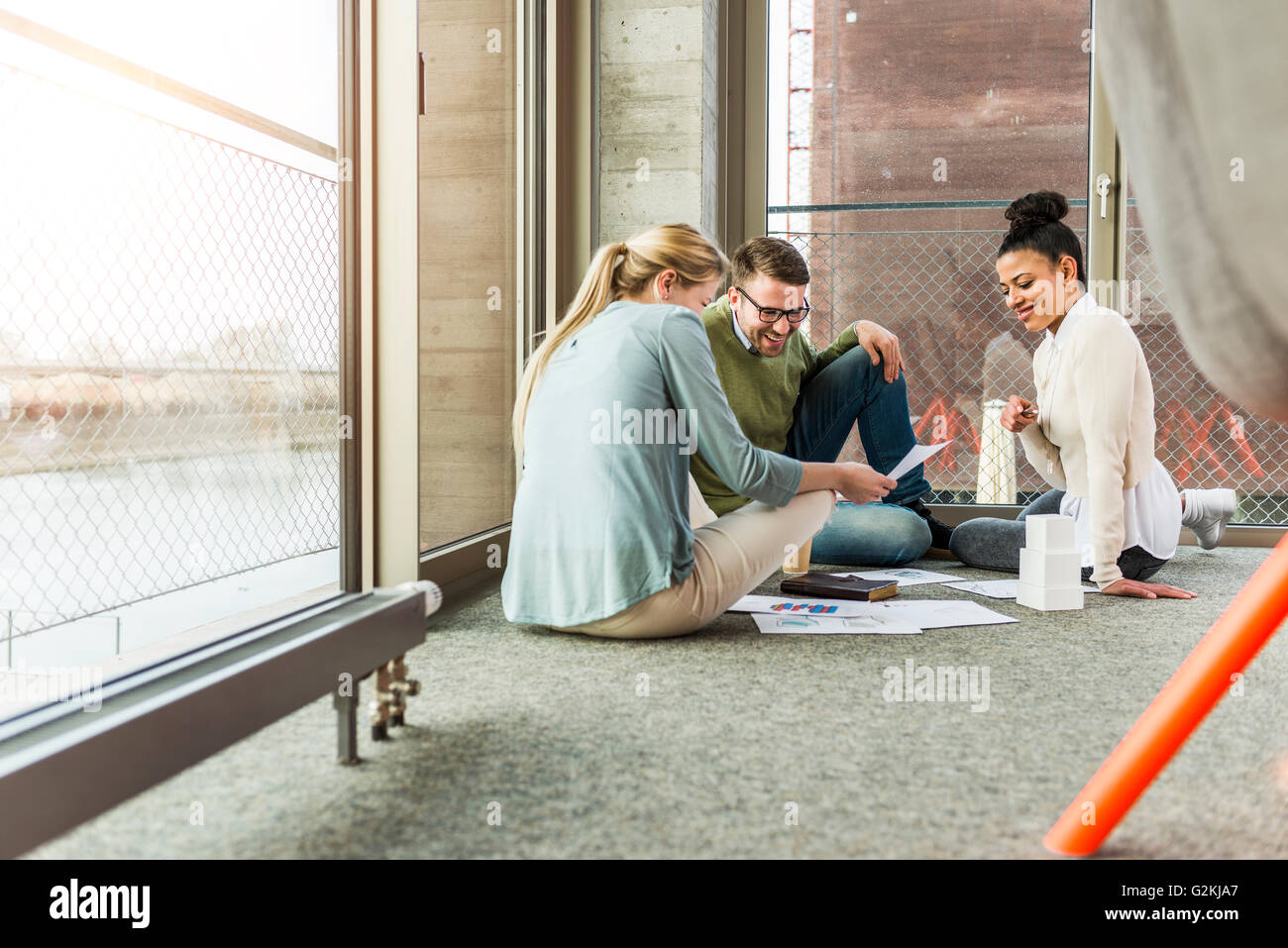 Three colleagues in office sitting on floor working together Stock ...