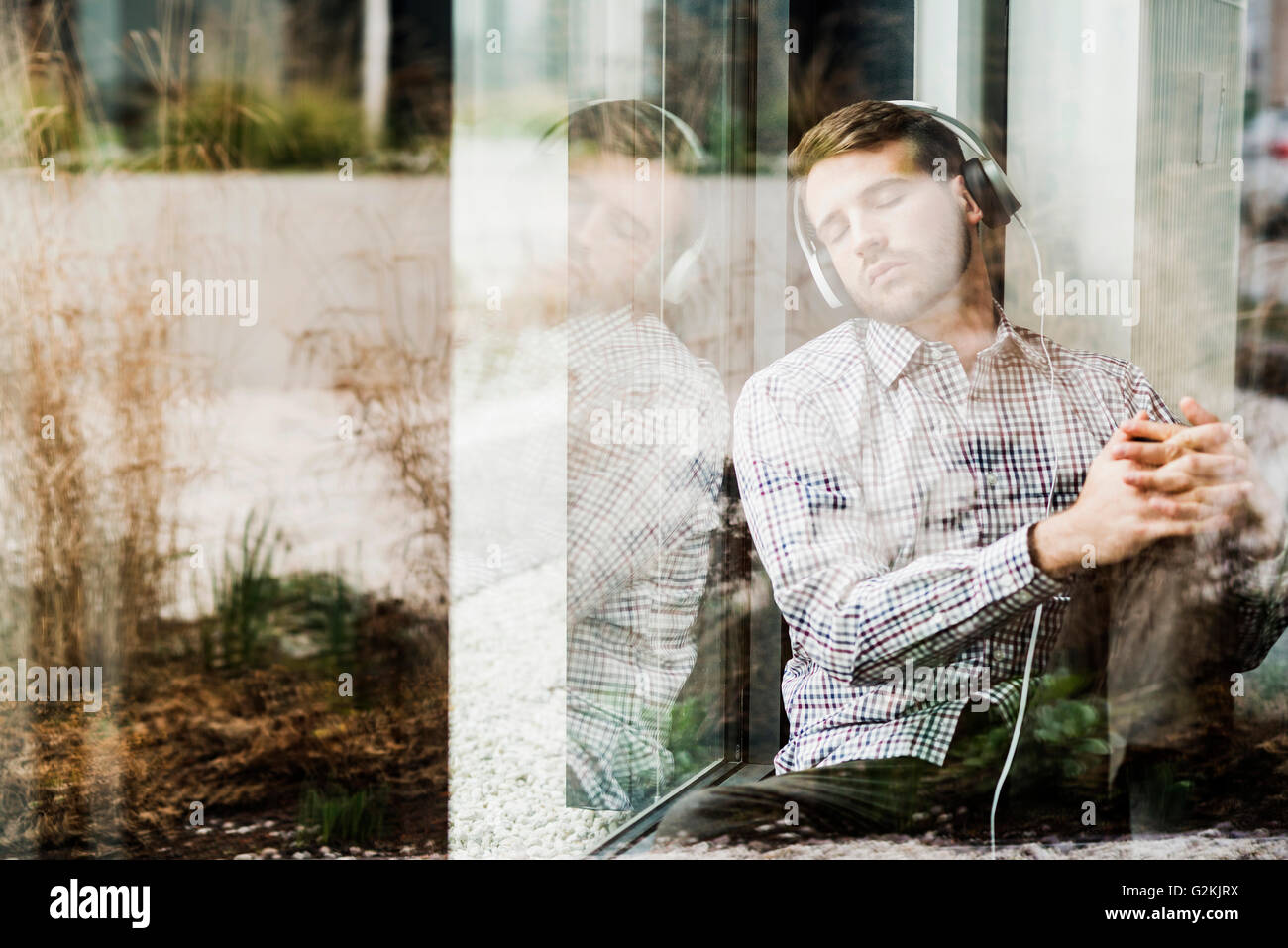 Young man sitting at the window wearing headphones Stock Photo - Alamy