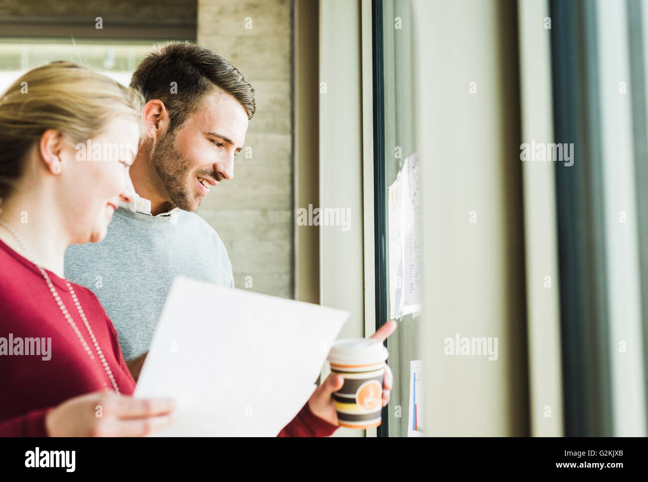 Two colleagues at office window looking at papers Stock Photo - Alamy