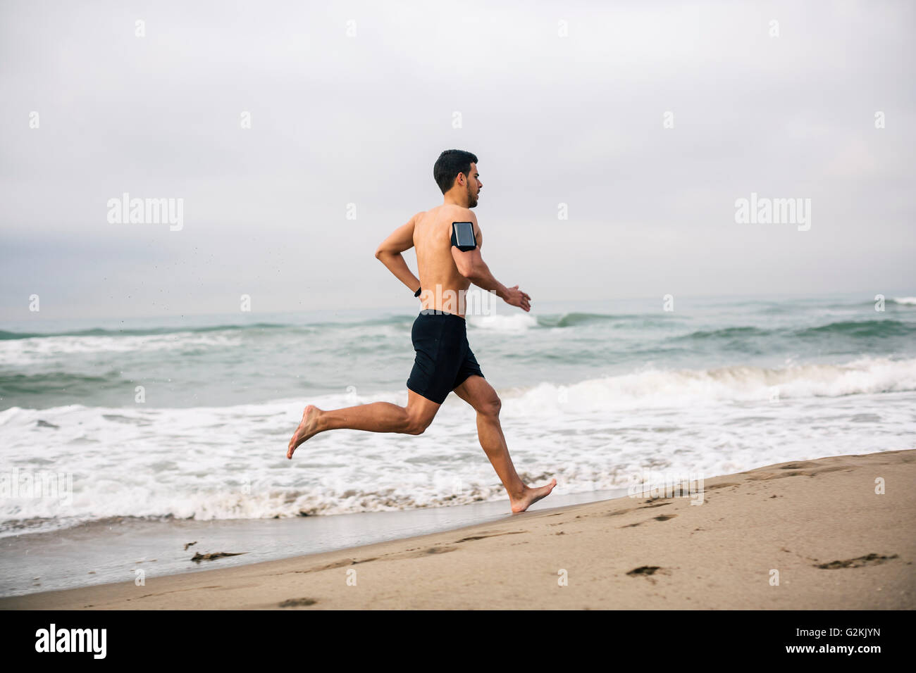 Young man running on the beach Stock Photo - Alamy
