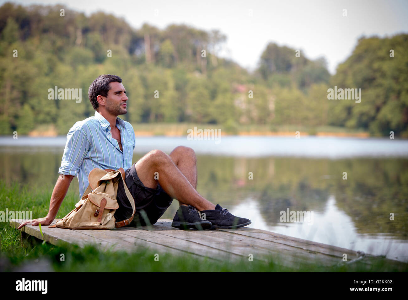 Portrait of young man sitting on a jetty at lake Stock Photo - Alamy