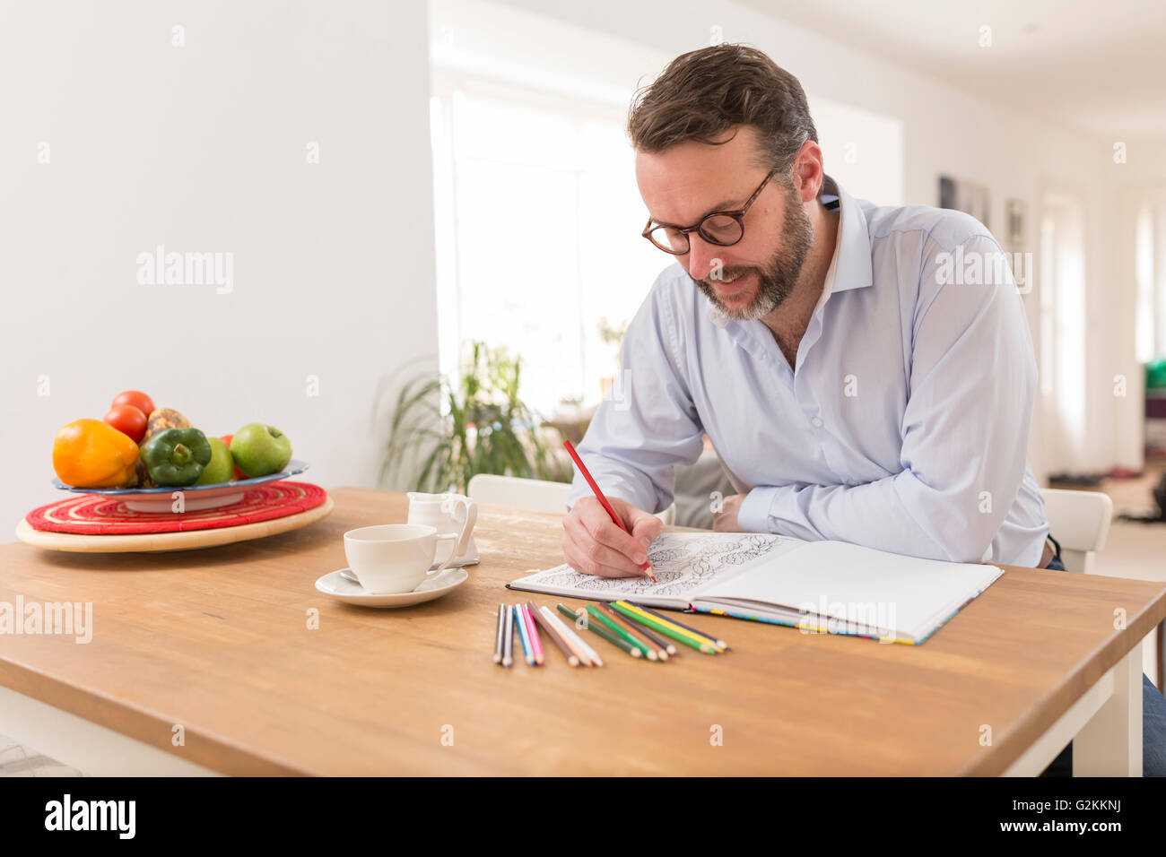 Man with colouring book and coloured pencils sitting at wooden table ...