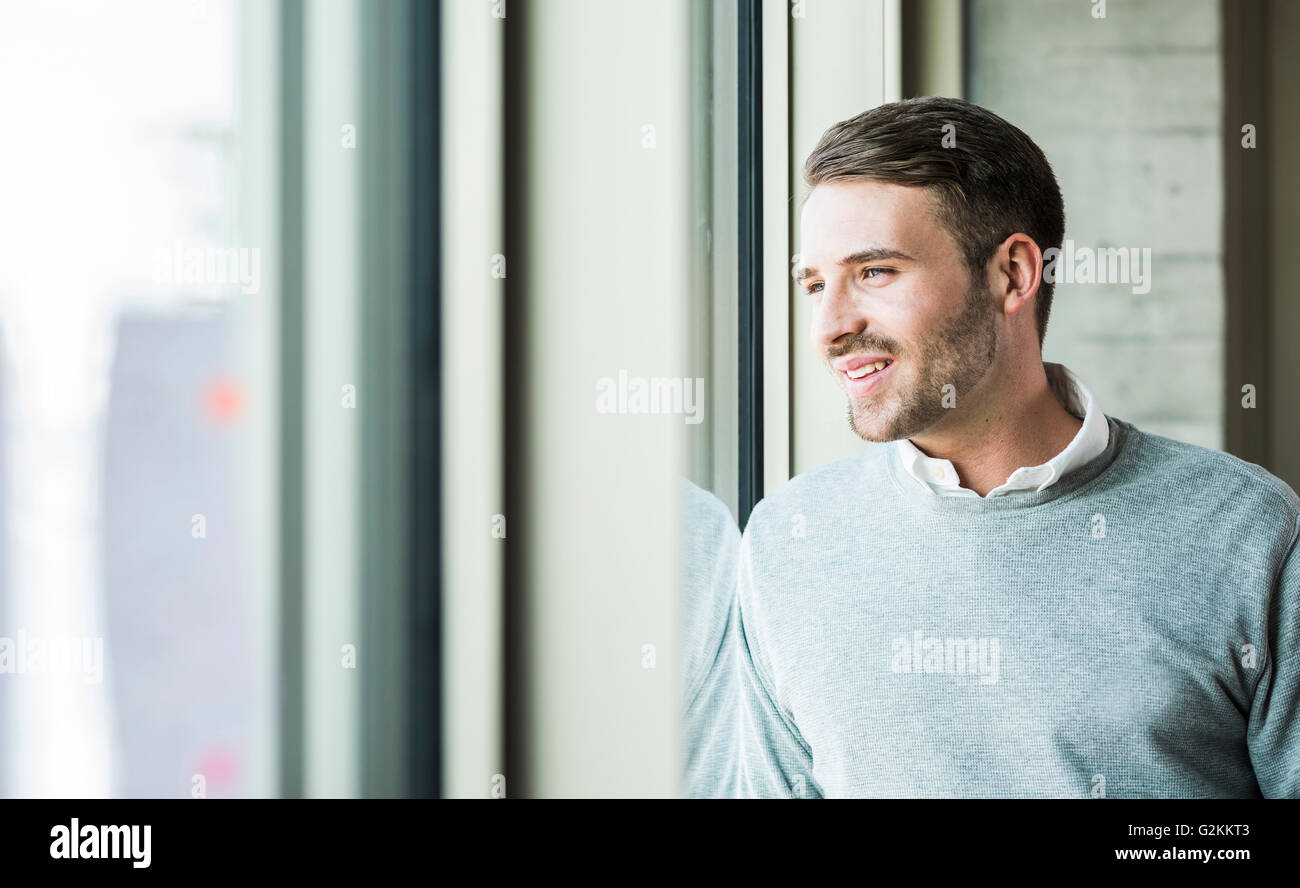 Smiling young man looking out of window Stock Photo - Alamy