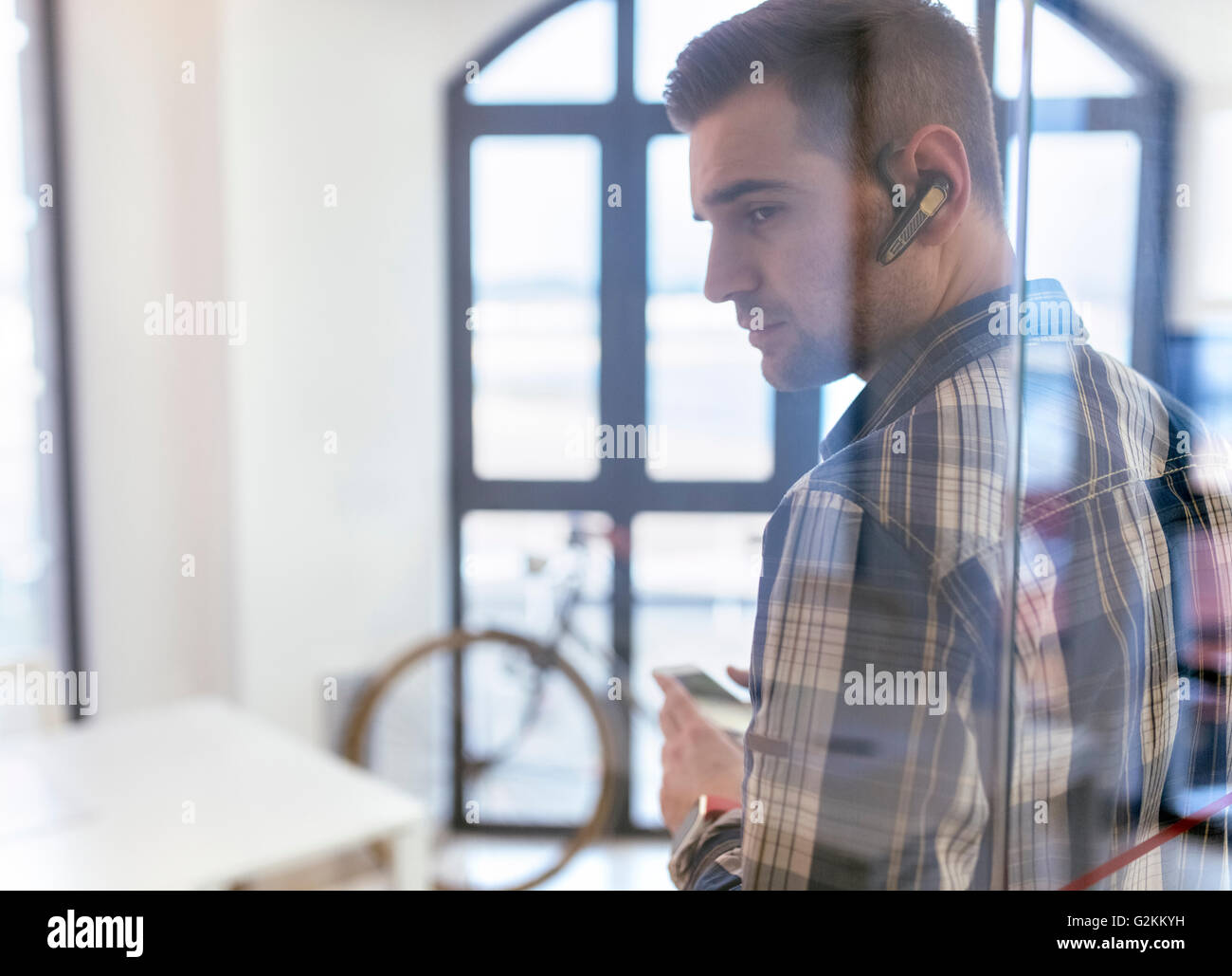 Young man wearing bluetooth headset in office Stock Photo - Alamy