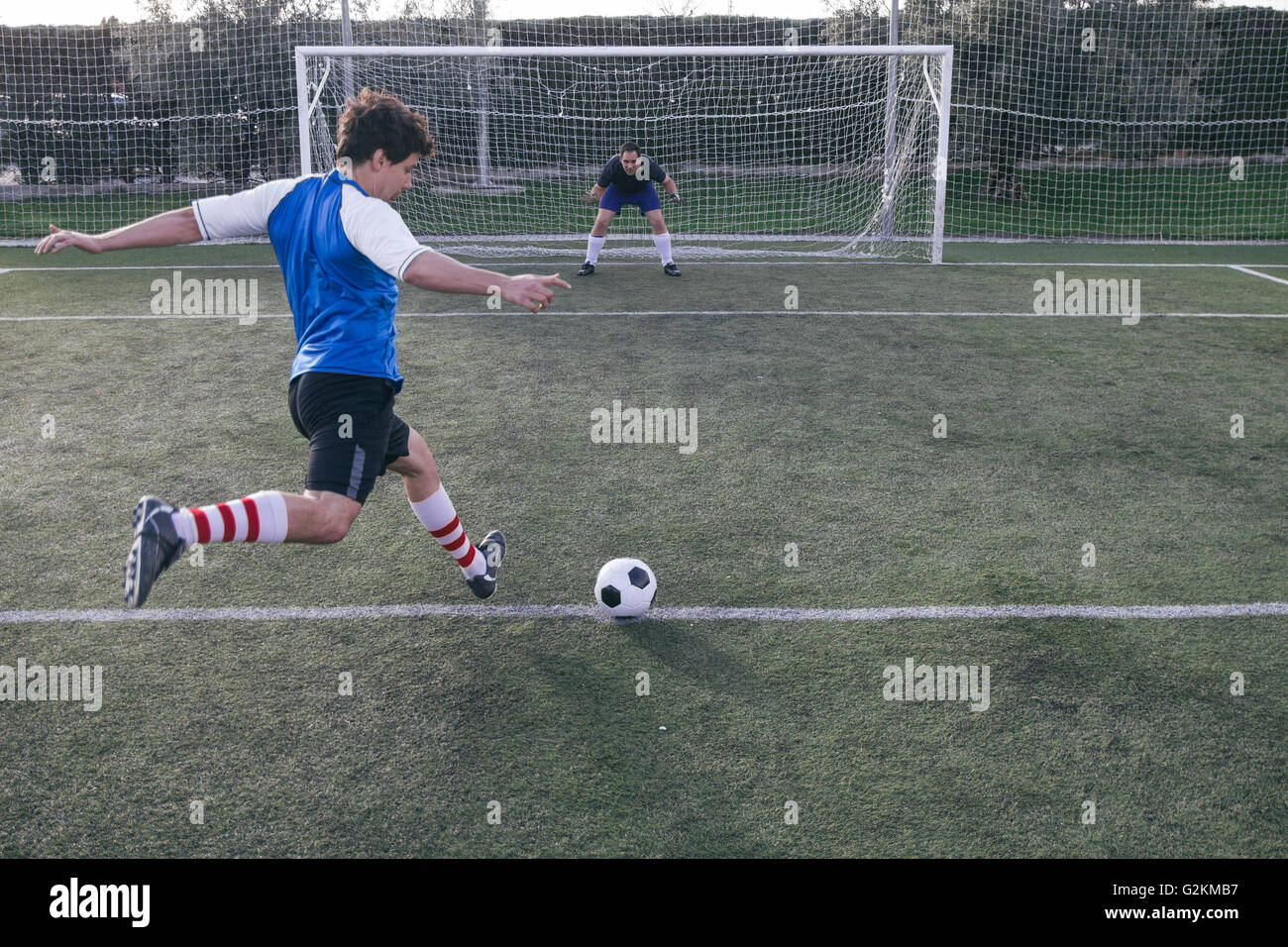 Football player kicking a ball in front of a goal with a goalkeeper ...