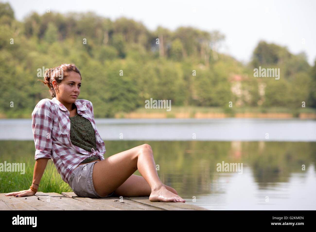 Portrait of young woman sitting on a jetty at lake Stock Photo - Alamy