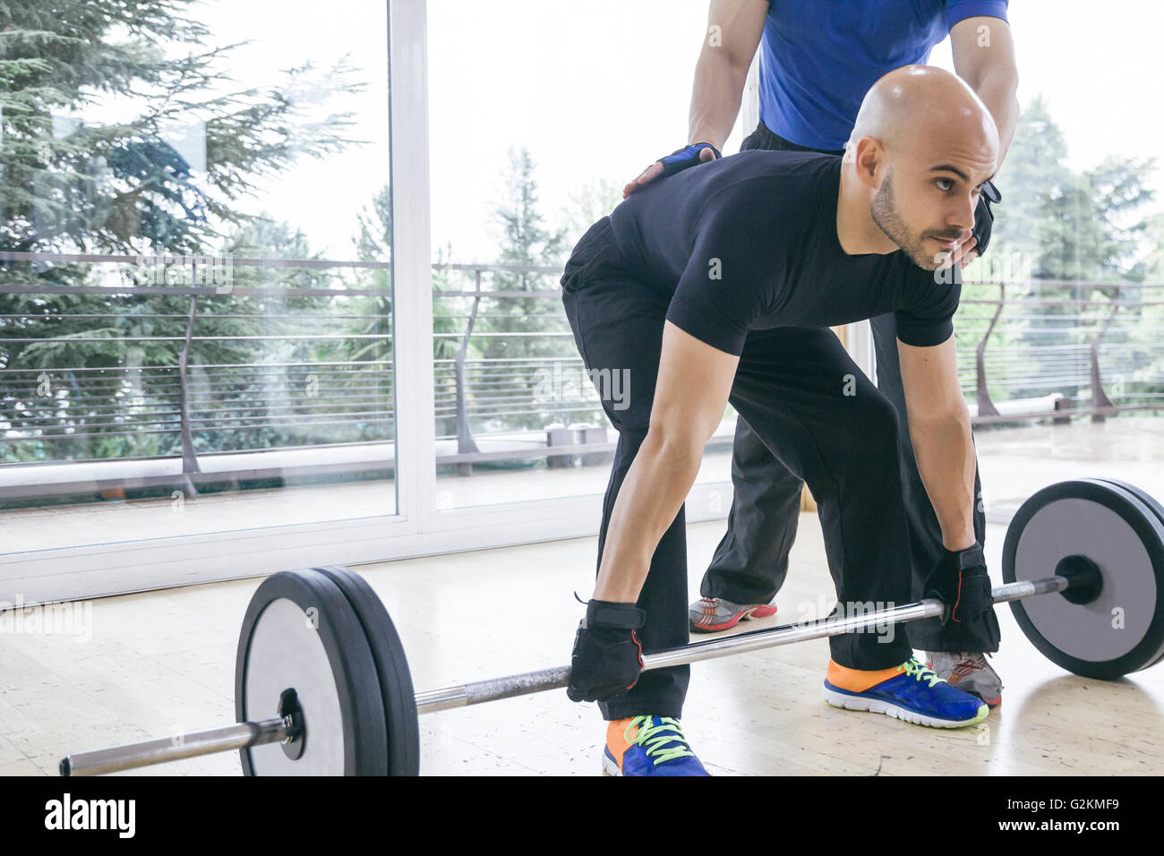 Man ready to lift a barbell assisted by a trainer Stock Photo - Alamy