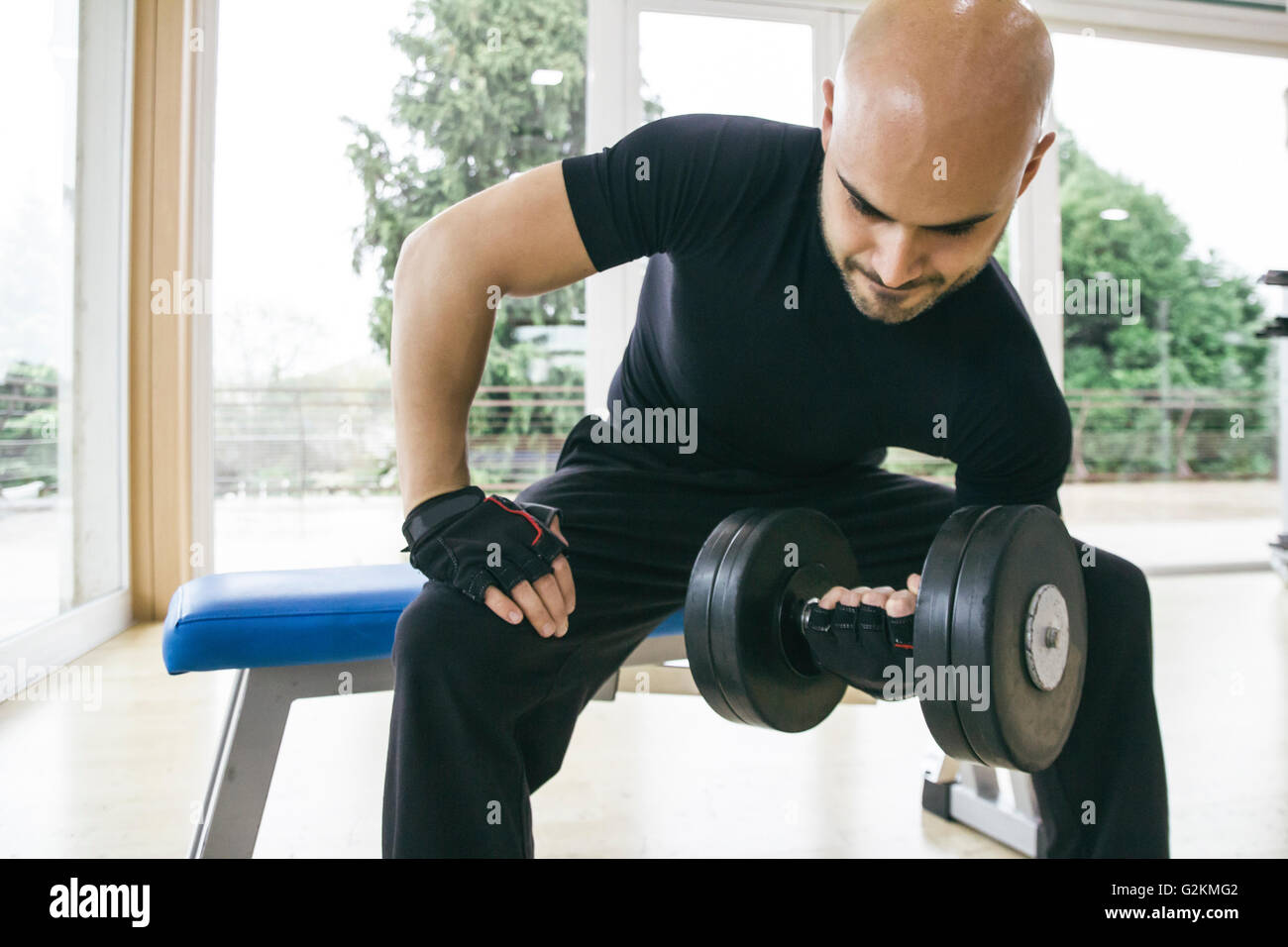 Man lifting a dumbbell sitting on a bench in a gym Stock Photo - Alamy