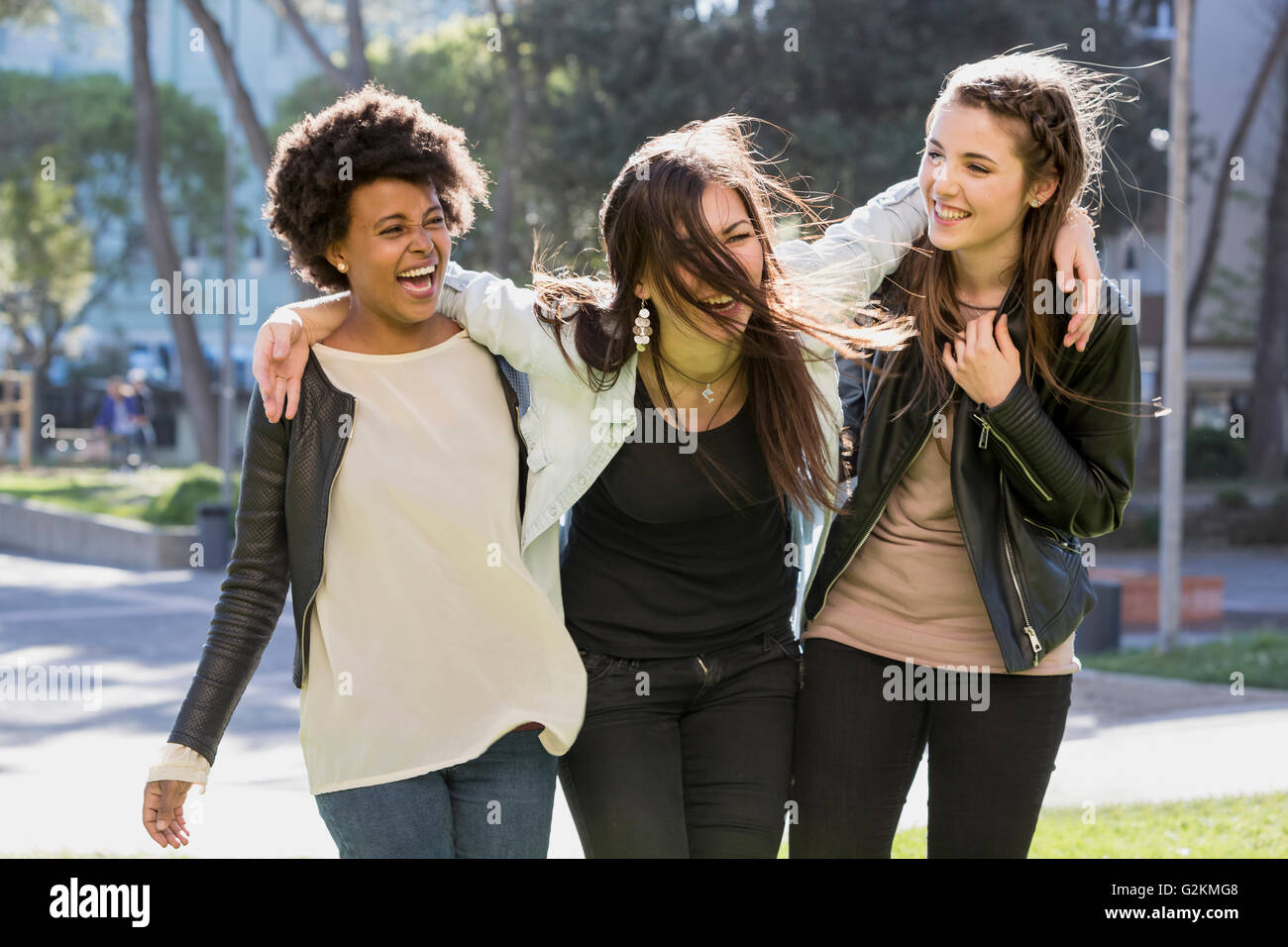Three young women walking arm in arm in the street Stock Photo - Alamy