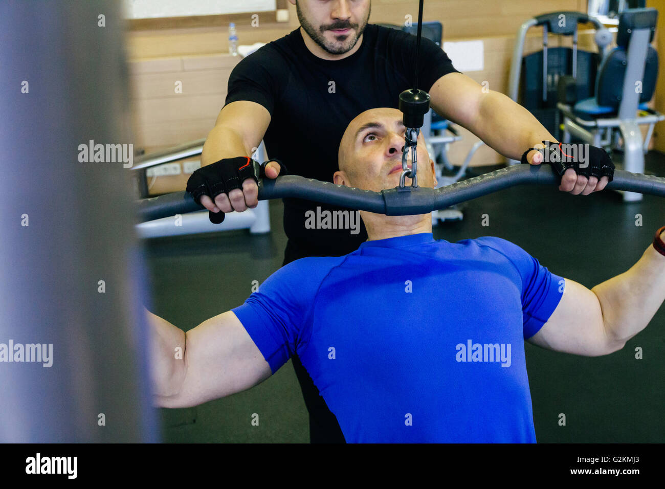 Man doing chest exercises in a gym machine assisted by his trainer ...