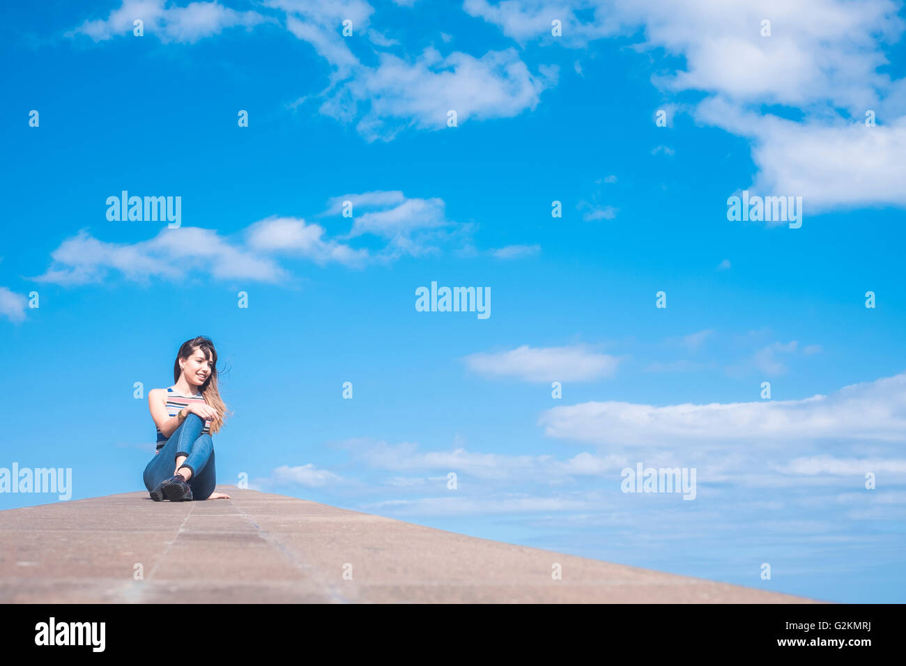 Smiling teenage girl sitting on wall under sky with clouds Stock Photo ...