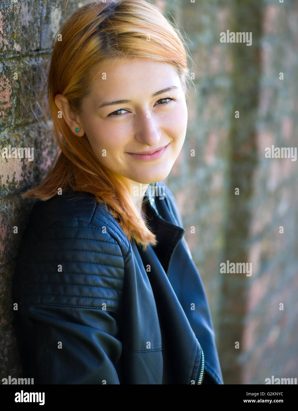 Portrait of a smiling, beautiful young woman leaning against a wall ...