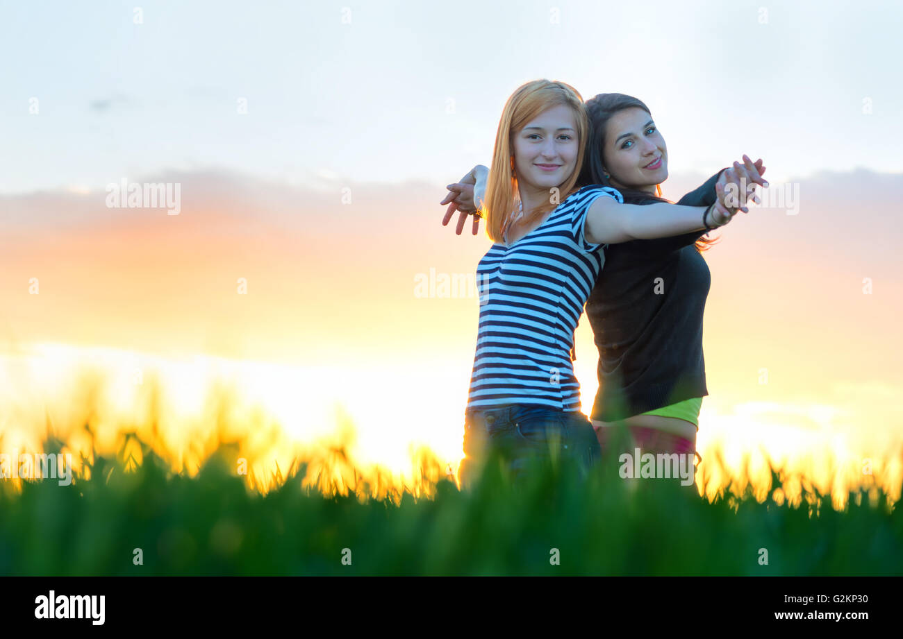 Two young women hugging and rest in the rays of sunset outdoors. Best ...