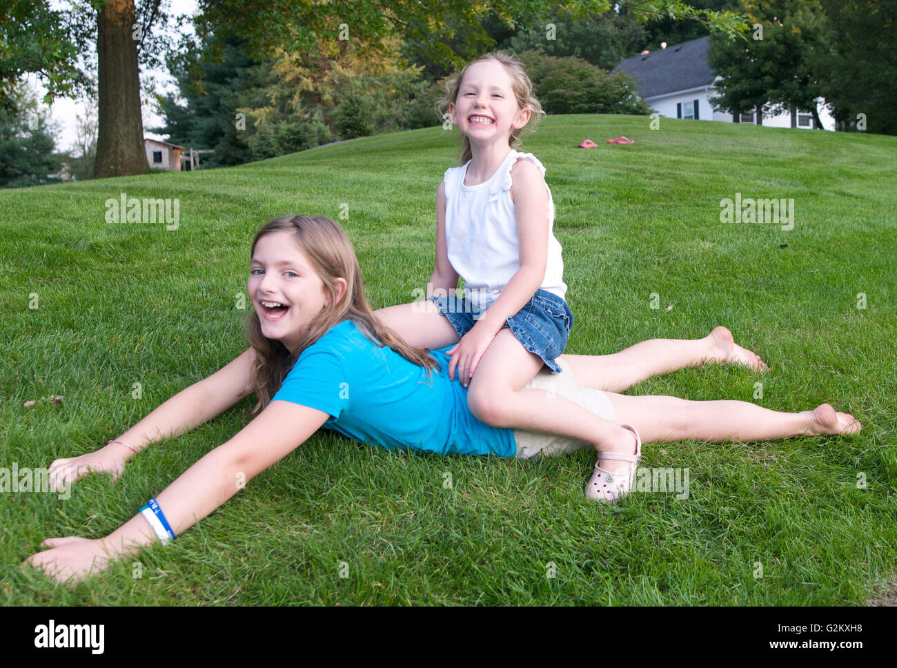 Smiling Young Girl Laying on Ground With Another Girl Sitting on Her ...