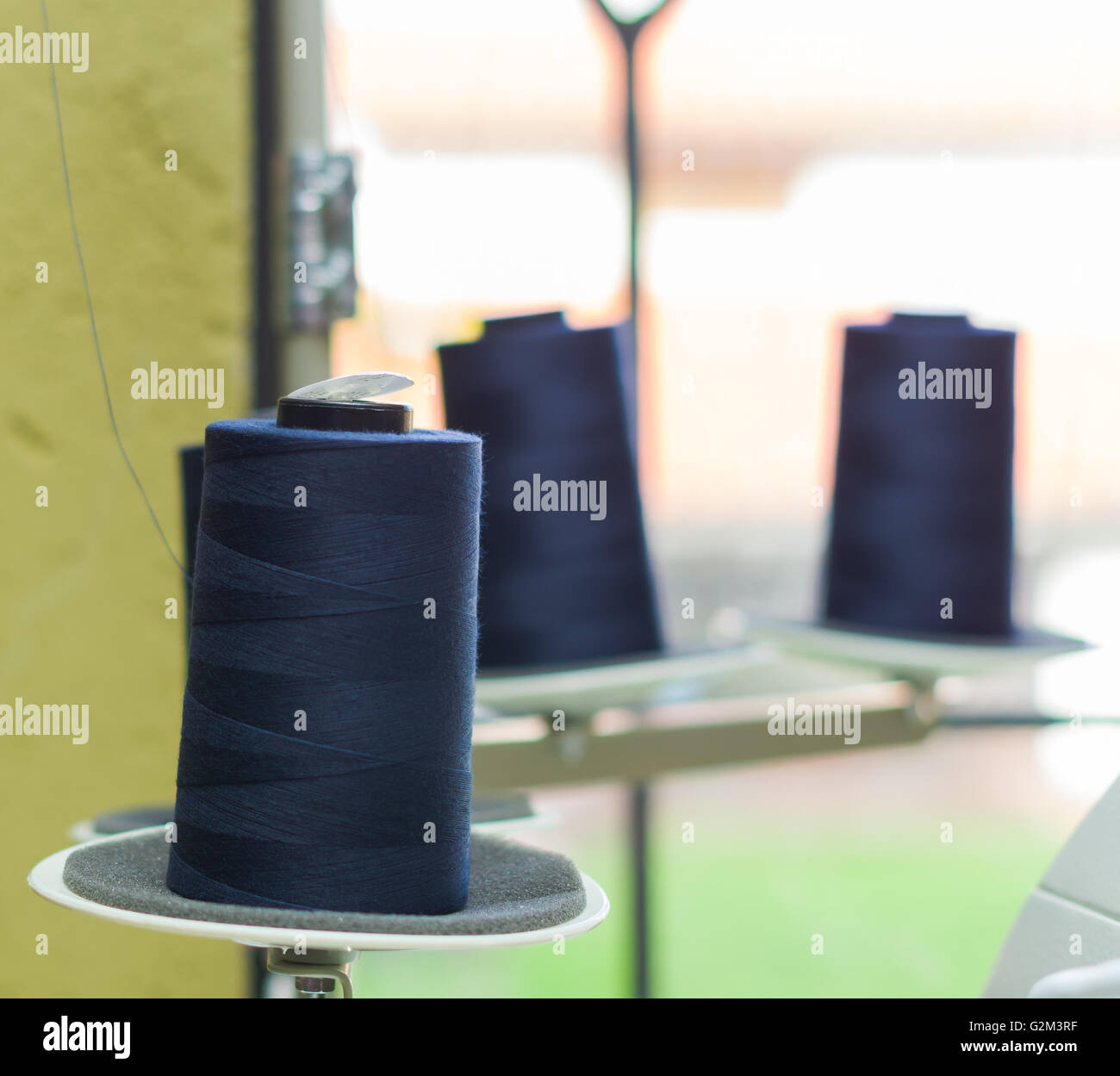 Blue spool of thread ready to be used in a sewing machine, behind other ...