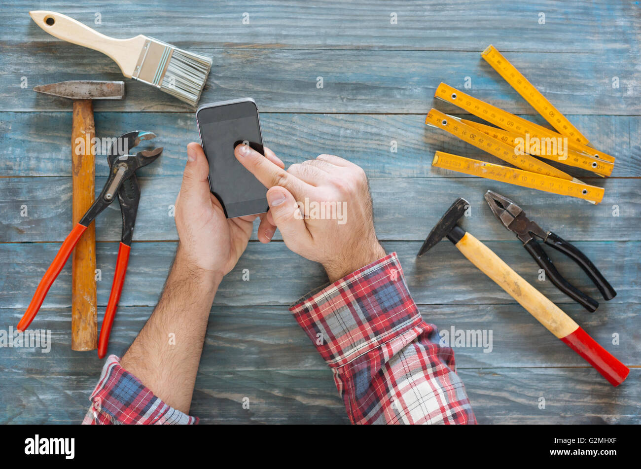 Man working on a DIY project with his phone, wood shavings and ...