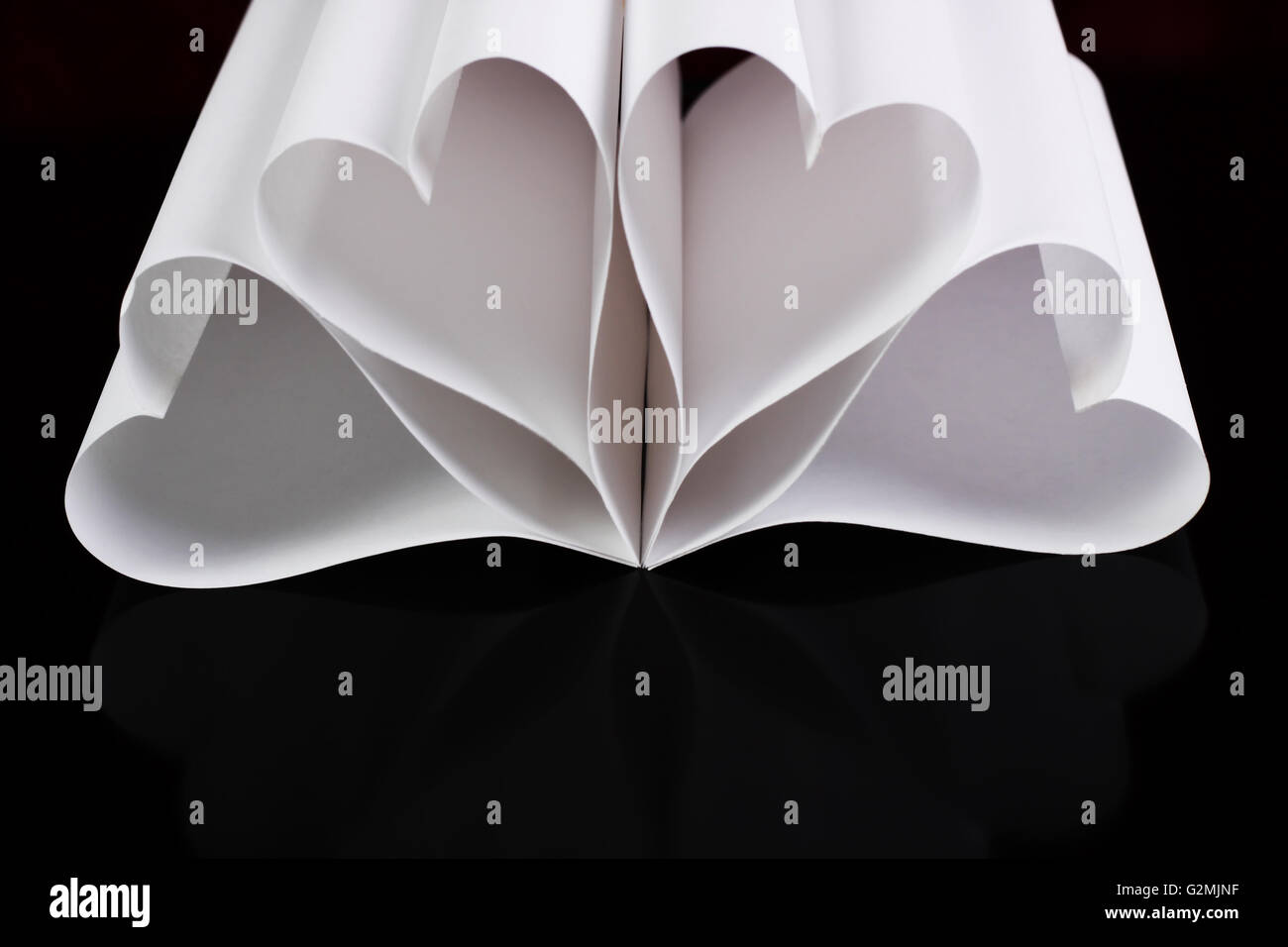 white paper hearts in a flower shape on black table with reflection ...