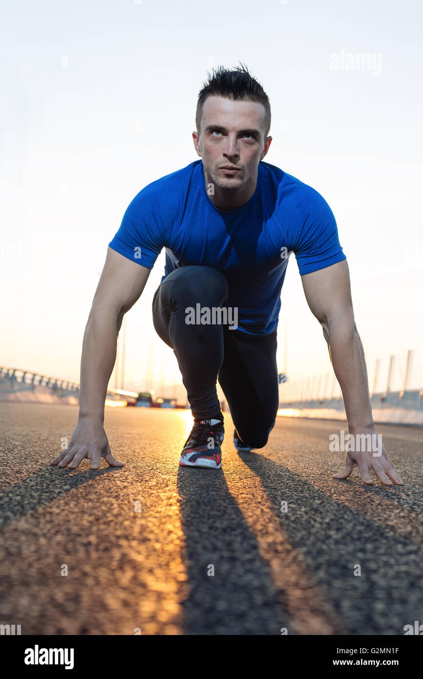 Portrait of a sports man in start position outdoors. Reading for run ...