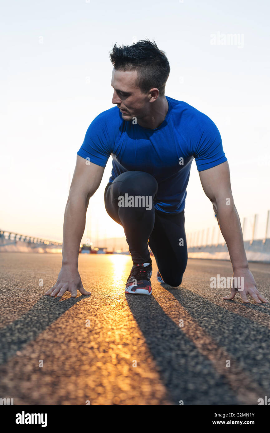 Portrait of a sports man in start position outdoors. Reading for run ...