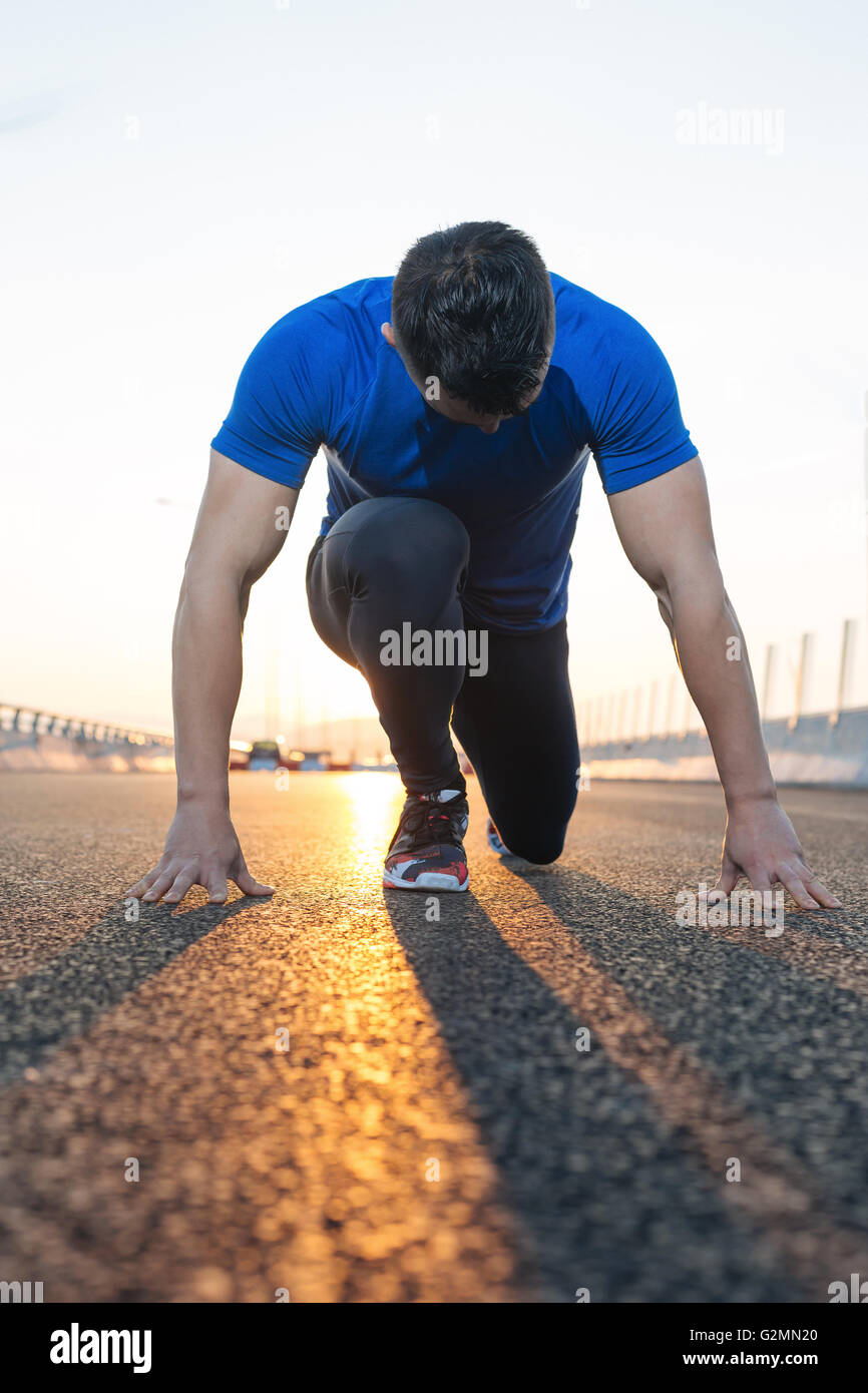 Portrait of a sports man in start position outdoors. Reading for run ...