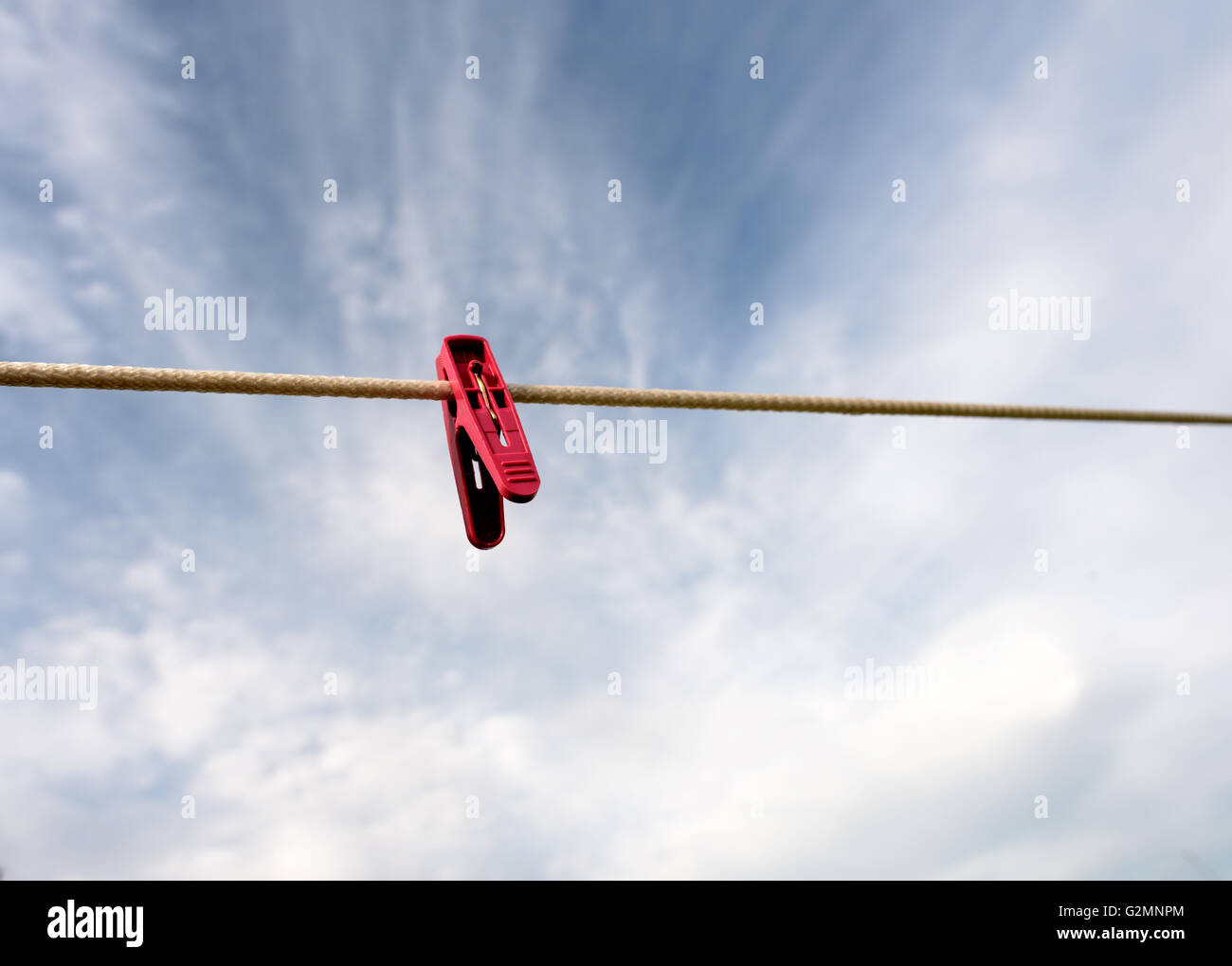 Single plastic red peg on a washing line set against a blue sky ...