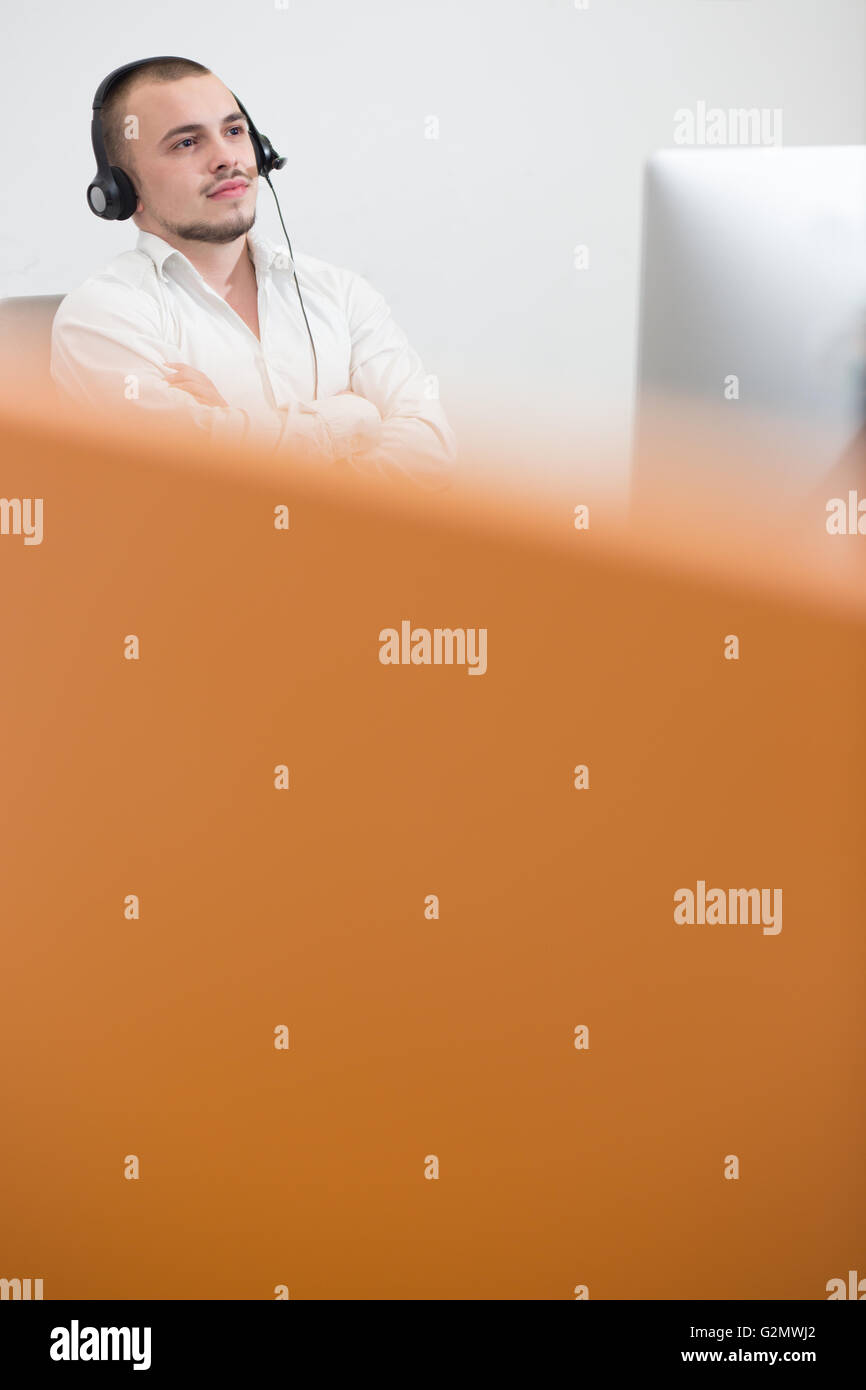 Smiling casual young man with headset using computer in a bright office ...