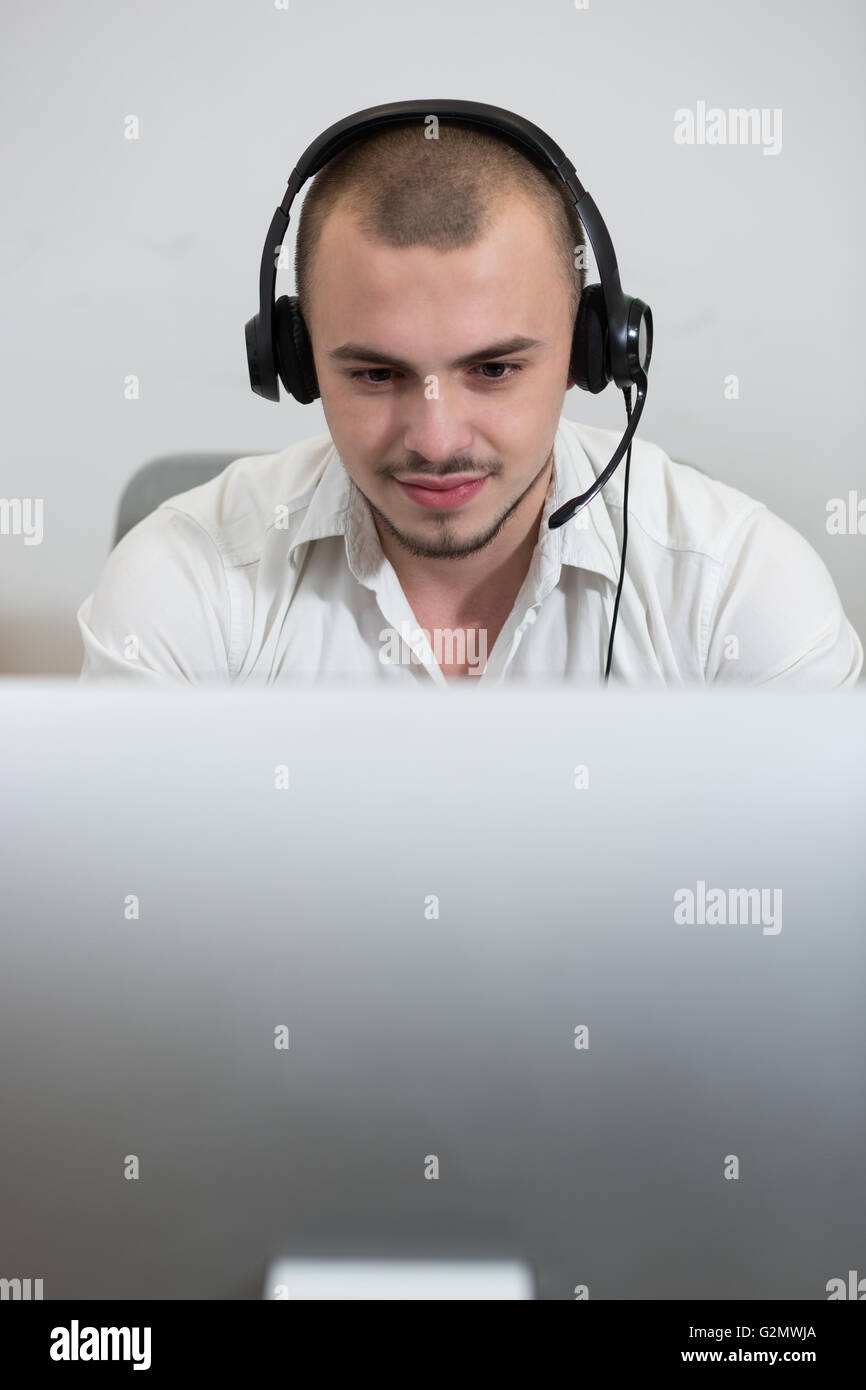 Smiling casual young man with headset using computer in a bright office ...