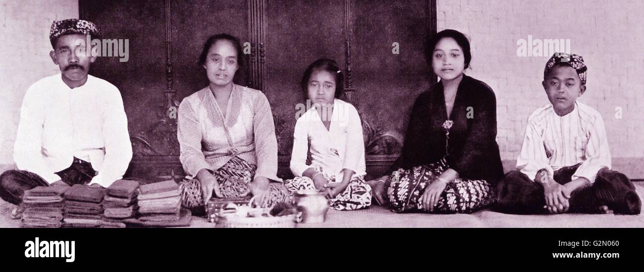 Photograph shows an Indonesian family seated in their house. The father ...