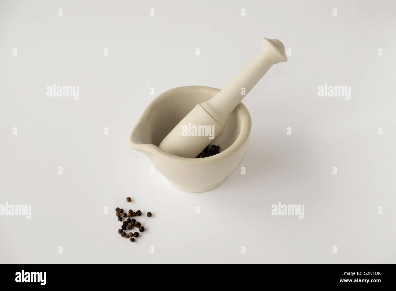Ceramic mortar and pestle with black peppercorns against plain white ...