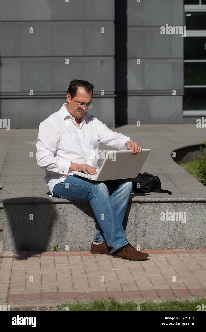 Adult man with computer sitting outdoors sunny day Stock Photo - Alamy