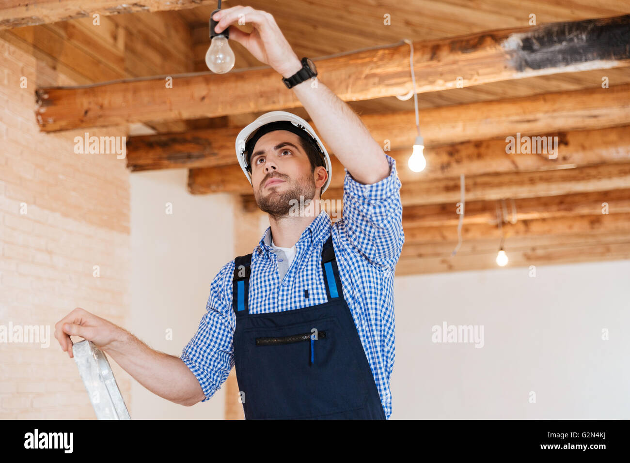 Handsome young builder fixing socket using ladder indoors Stock Photo ...