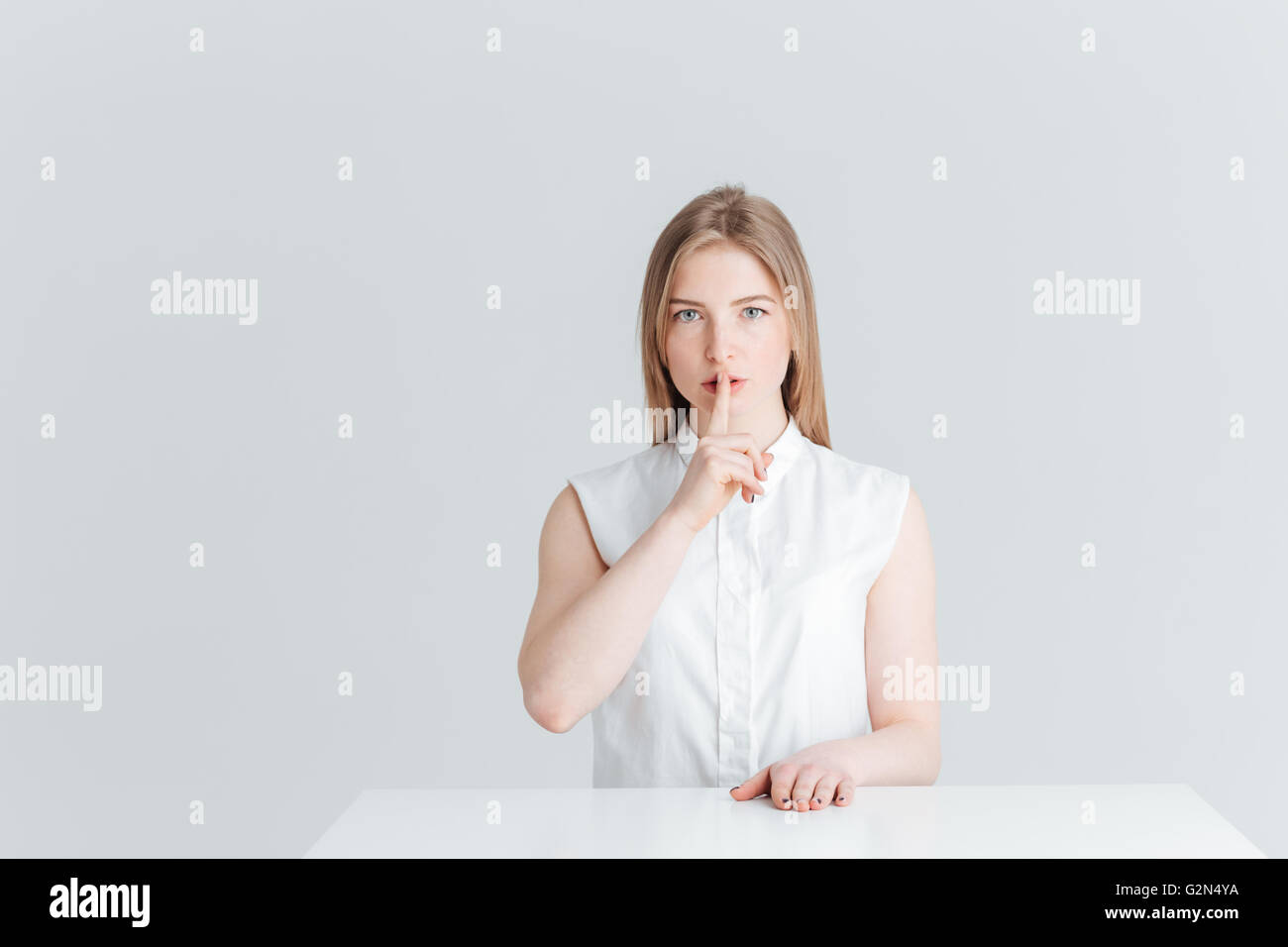 Young woman sitting at the table and showing finger over lips isolated ...