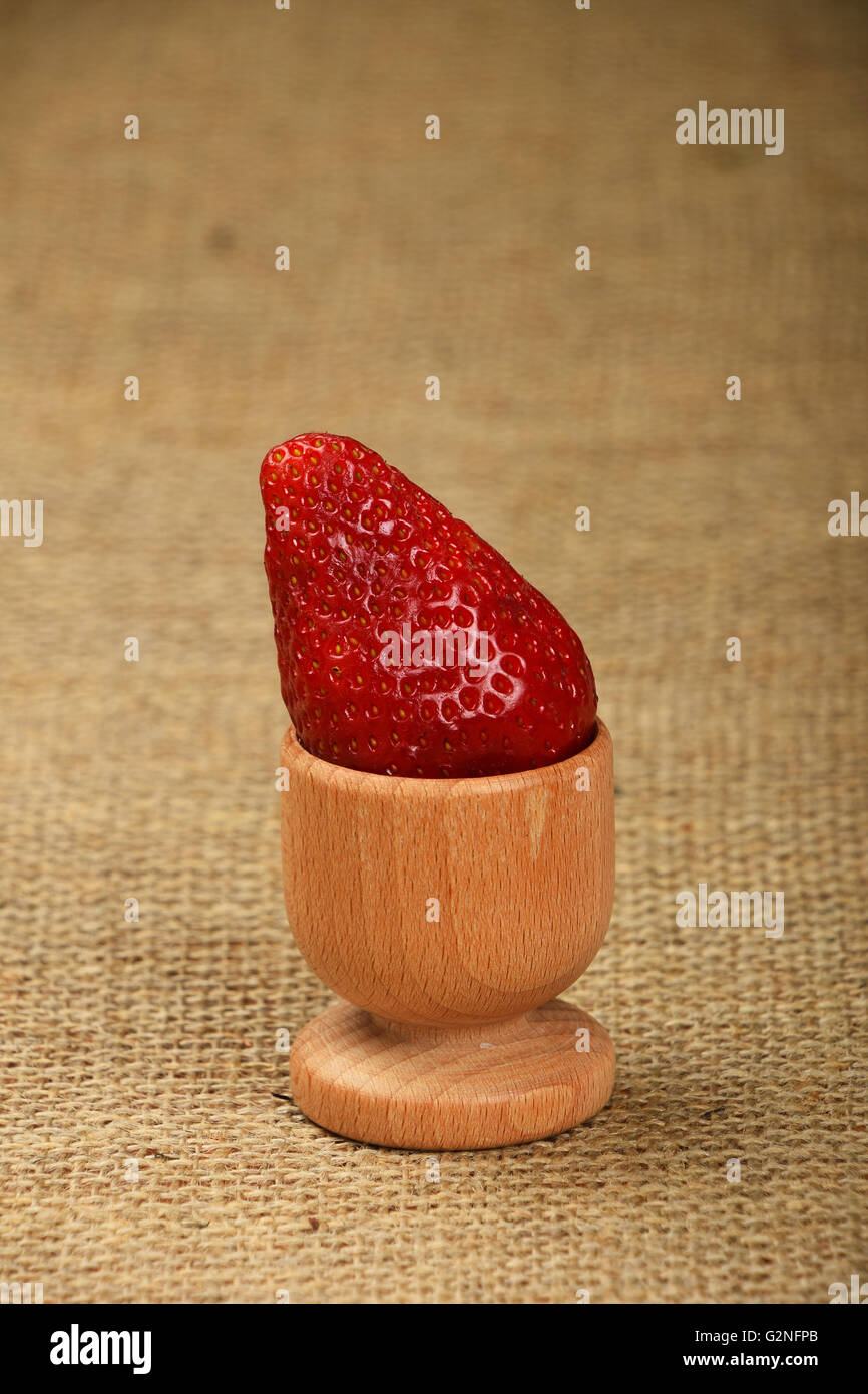 One big red mellow strawberry in wooden eggcup holder on natural burlap ...
