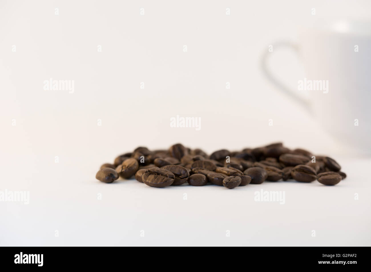 spilt coffee beans with white blurry cup in background Stock Photo - Alamy