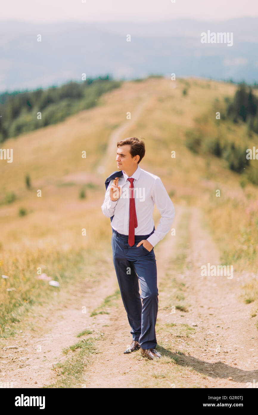 Young man in stylish suit walking on trail by summer field with his ...