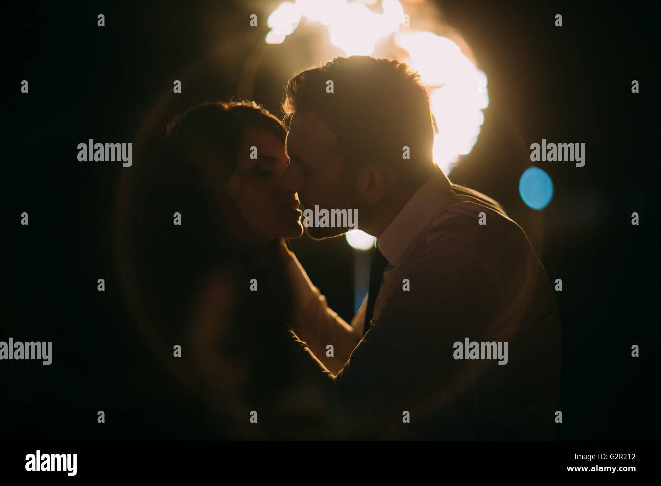 Romantic and emotional kiss of newlywed couple in front flaming heart ...