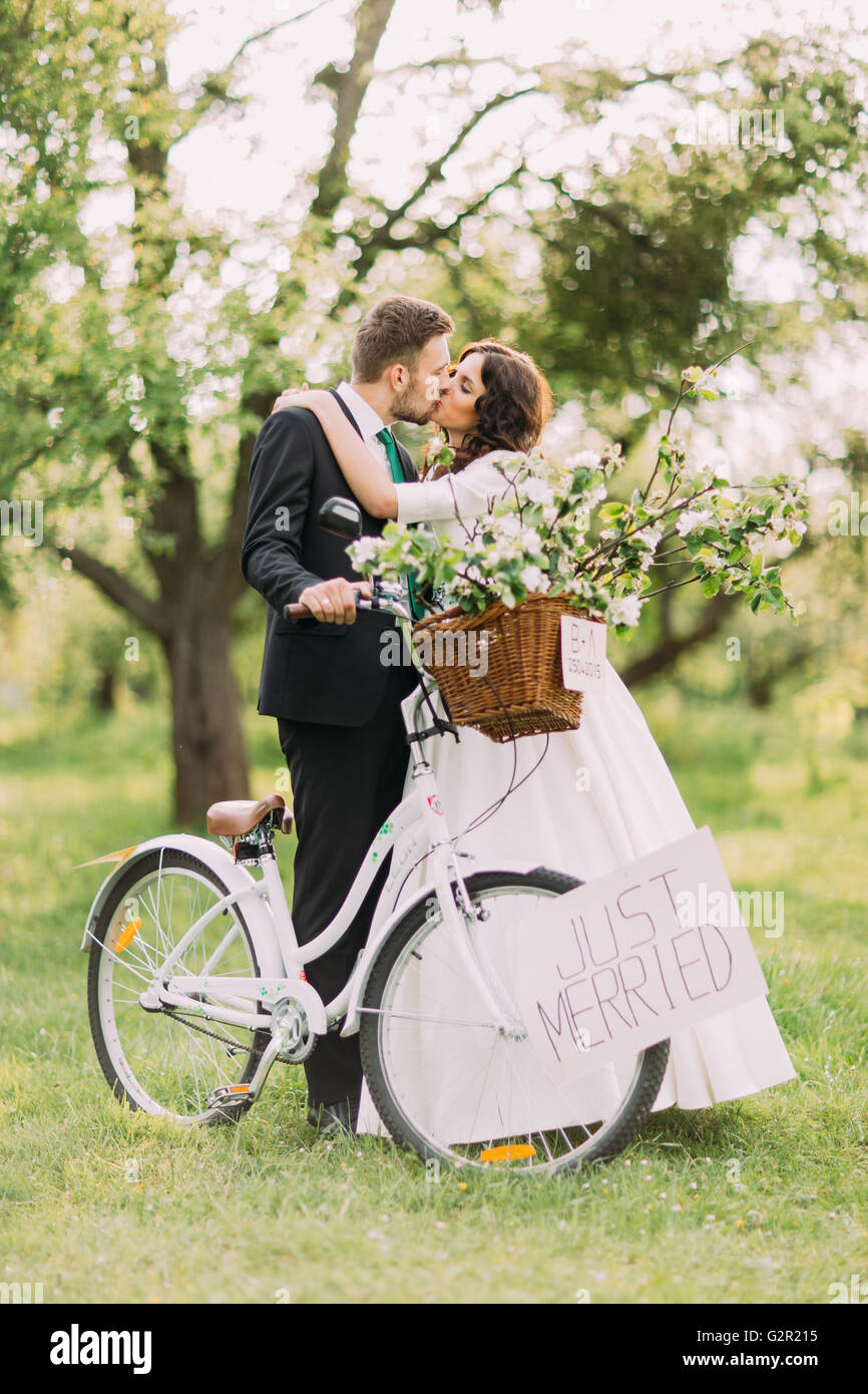 Sensual young newlywed couple kissing in park with groom holding bicycle Stock Photo - Alamy