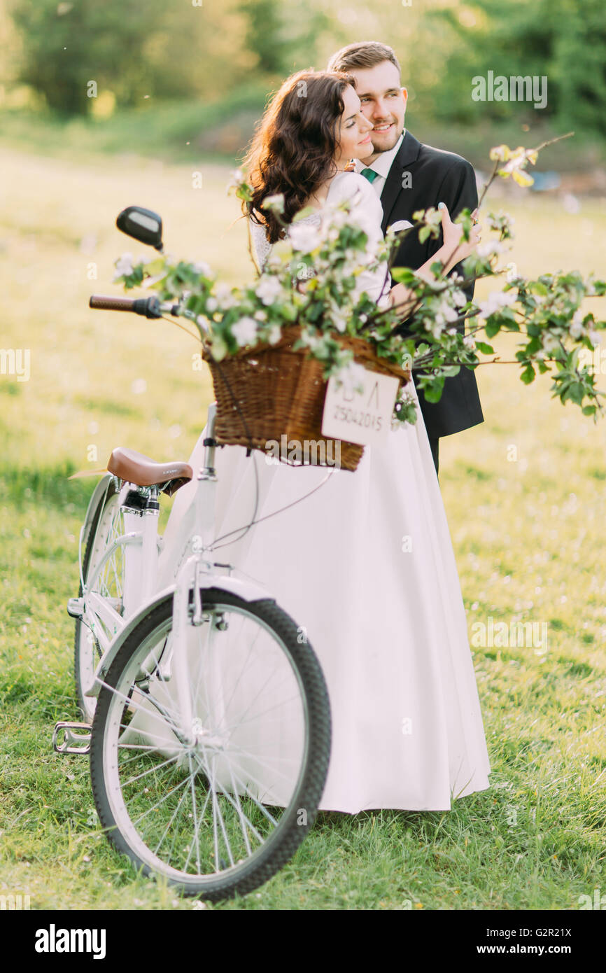 Happy newlyweds posing at park with bicycle in wedding decoration after ...