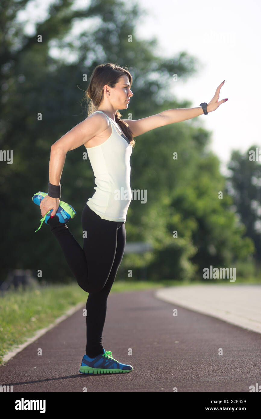 Girl stretching arm up, leg up, track Stock Photo - Alamy