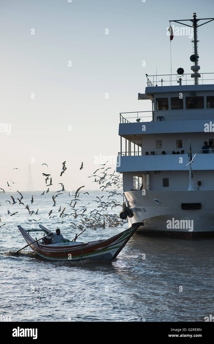 A traditional long boat passing by a passenger ferry at the Yangon ...