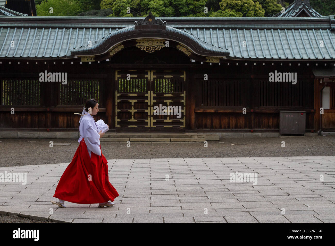 A shrine maiden in red and white robes in a courtyard at the ...