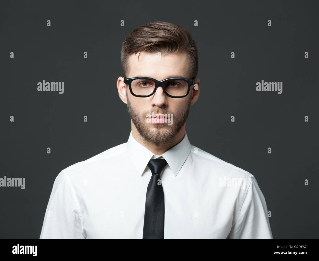 Portrait of handsome serious young businessman standing against dark ...