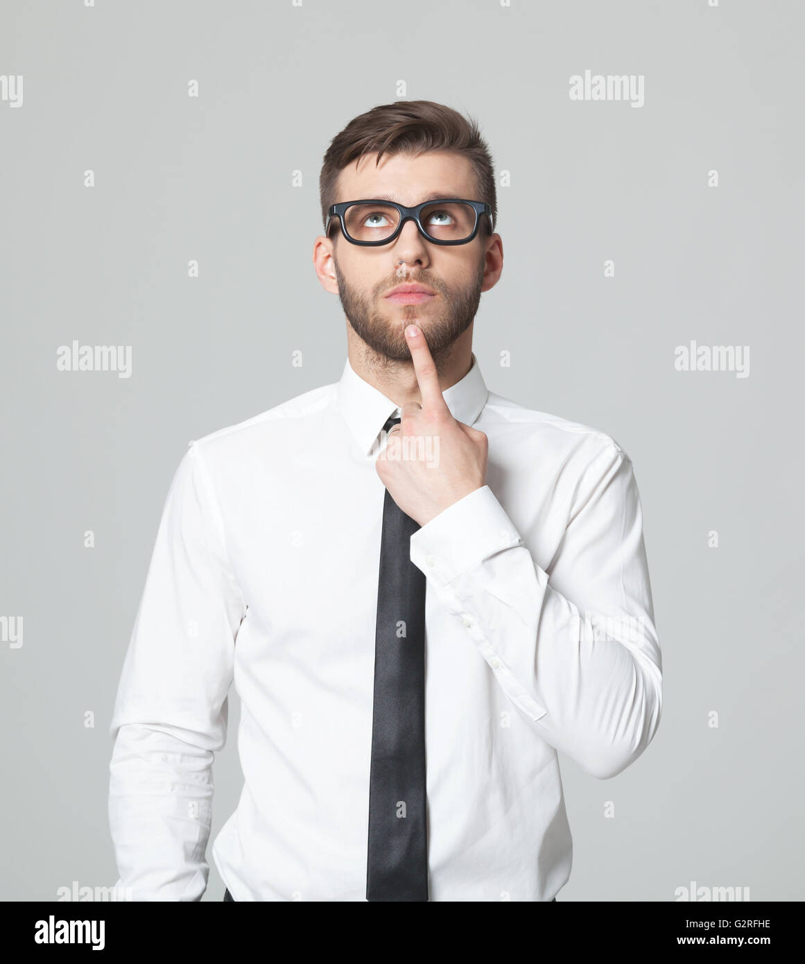 Young handsome businessman thinking while standing against gray ...