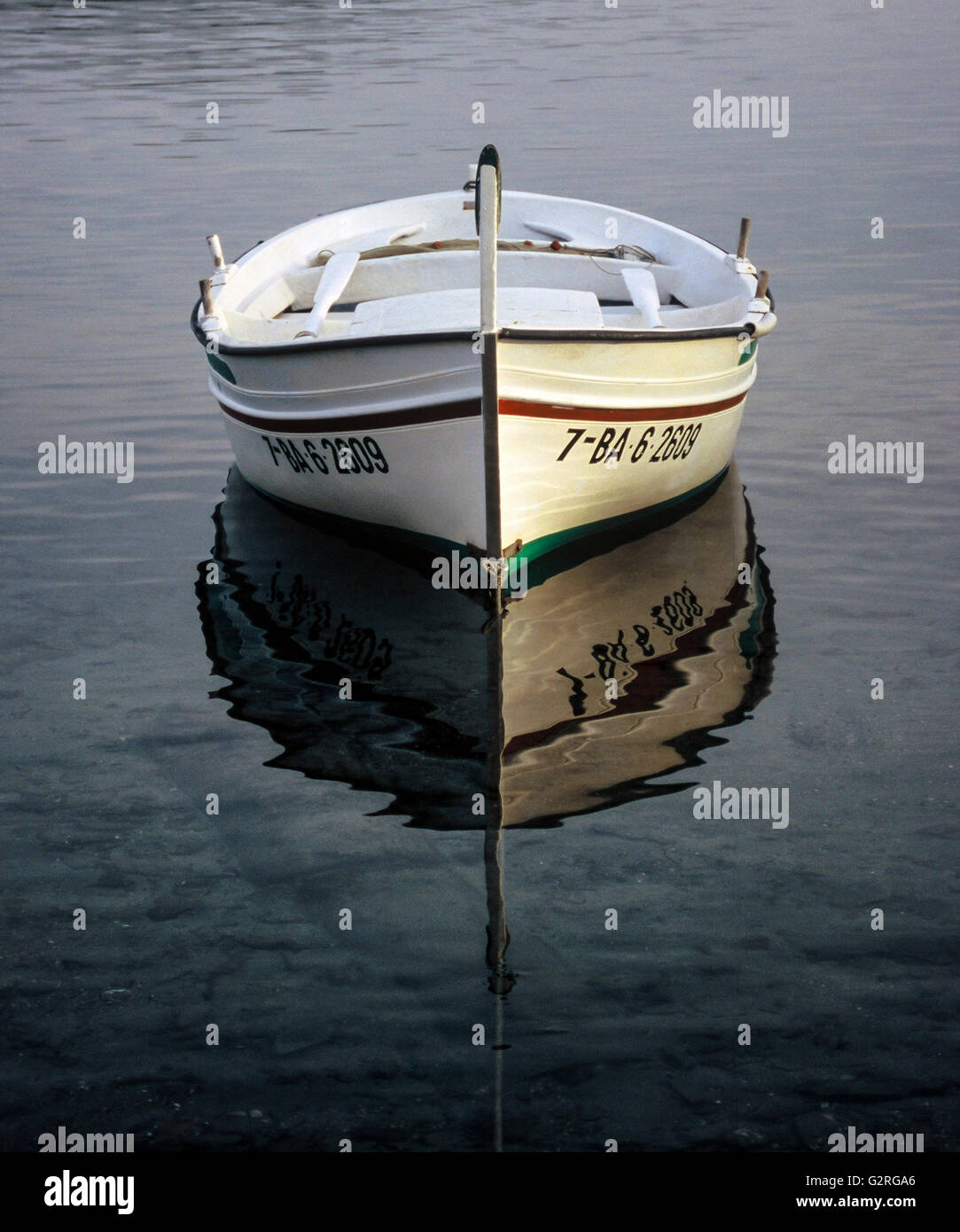 A small open boat reflects in the shallow, clear, blue water on the ...