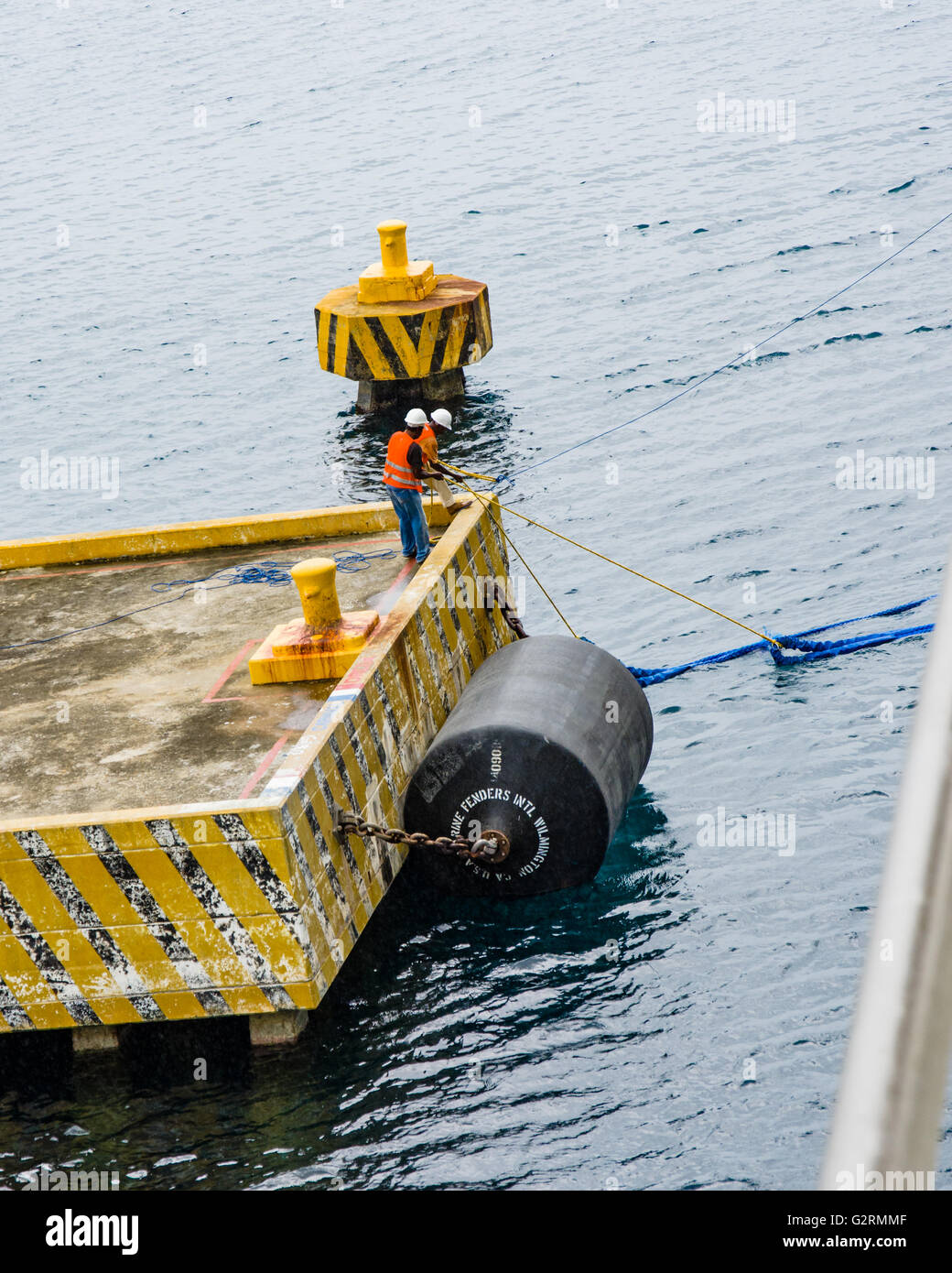 Workers pull ropes to assist a cruise ship docking at Port of Roatan ...